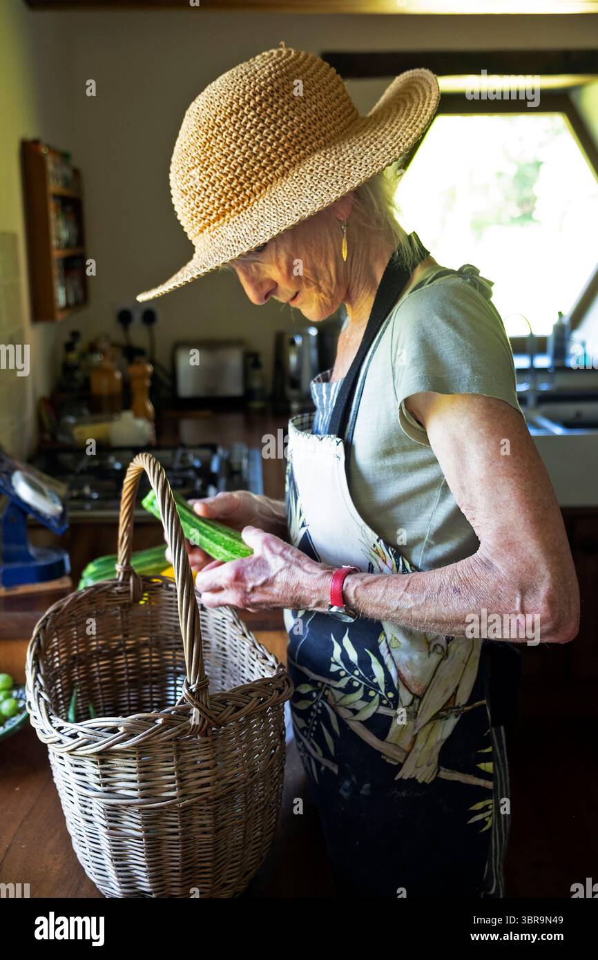 Older woman wearing straw hat apron standing in kitchen holding ...