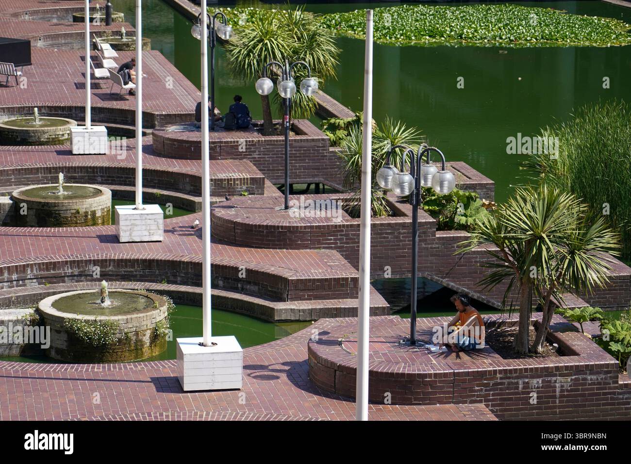 People sit near the artificial pond at Barbican Estate during a hot day ...