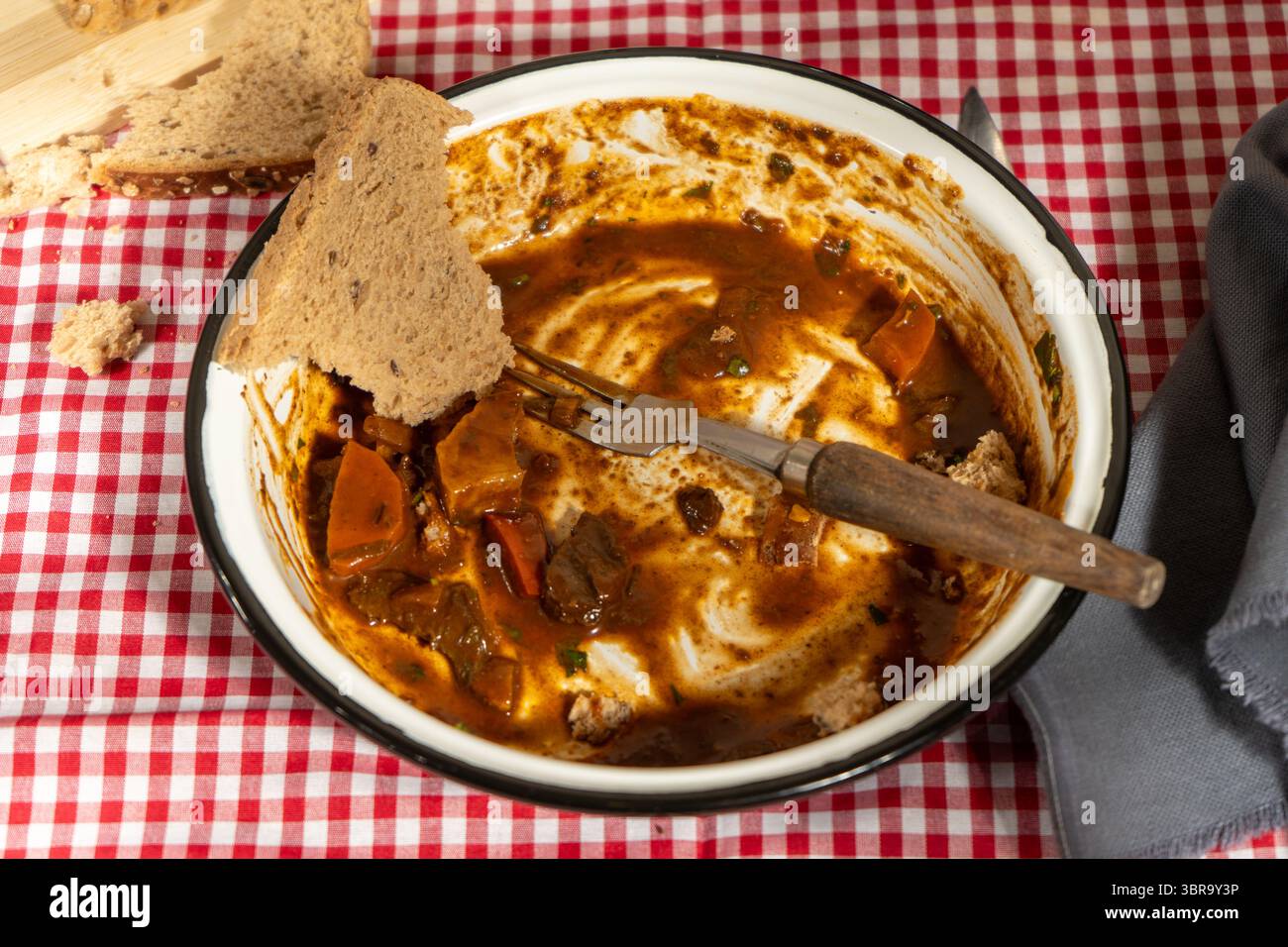 Savory beef stew remains with bread on a red checkered cloth Stock ...