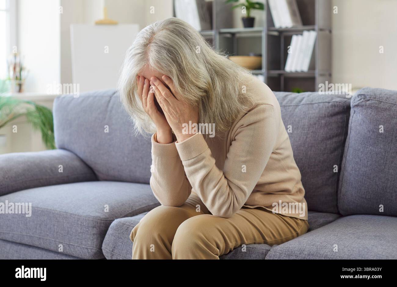Old senior woman sitting indoors on sofa in distress at home, covering ...
