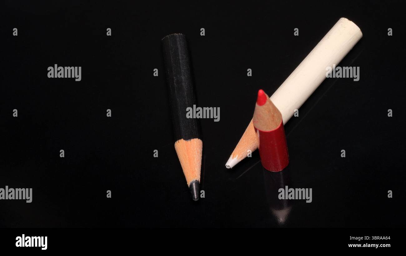 Three colored pencils rest on a reflective black surface, showcasing ...