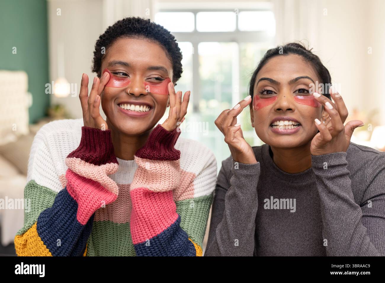 Diverse female friends applying red gel under-eye patches on couch in ...