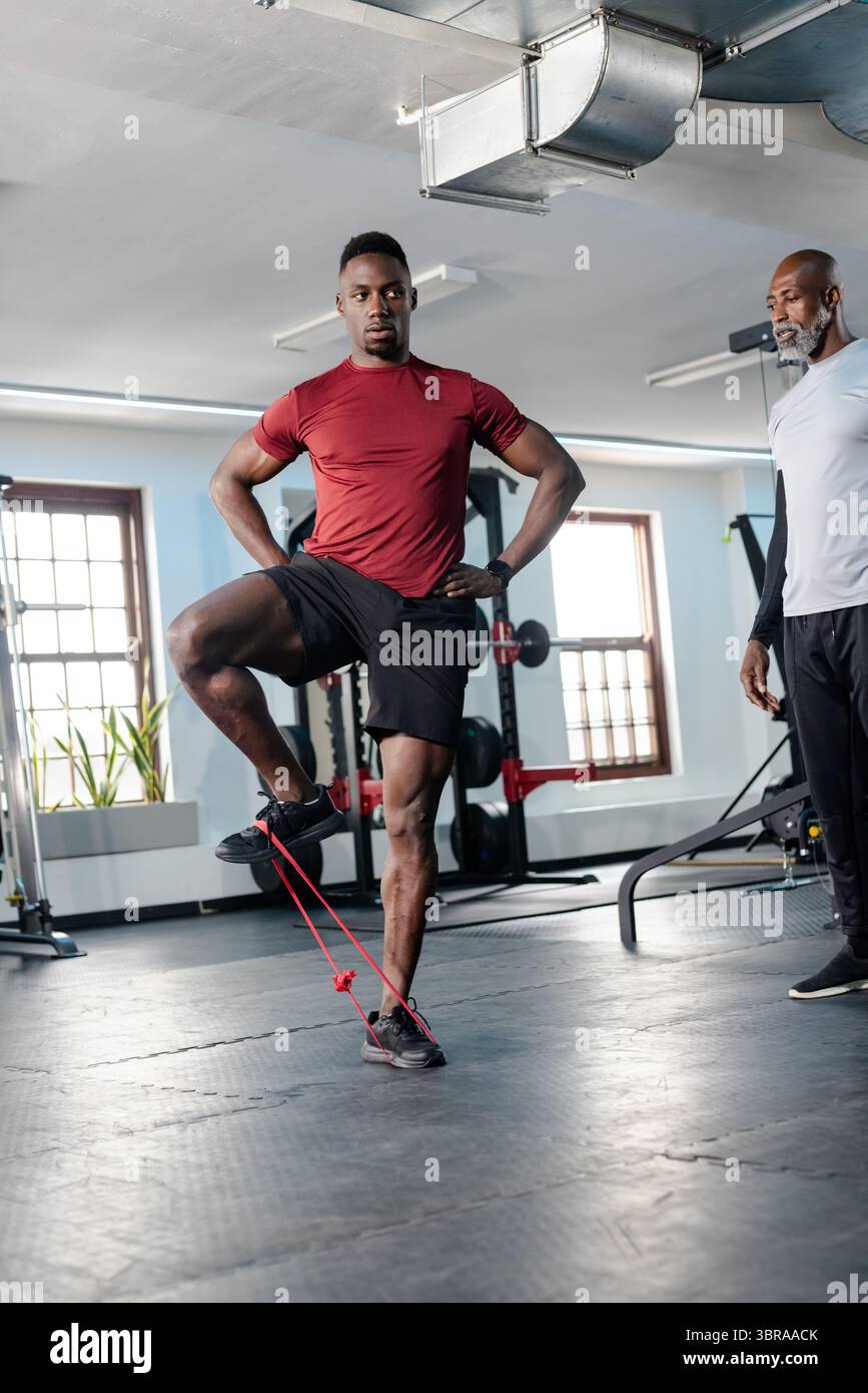 African American trainer guiding trainee balancing on red resistance ...