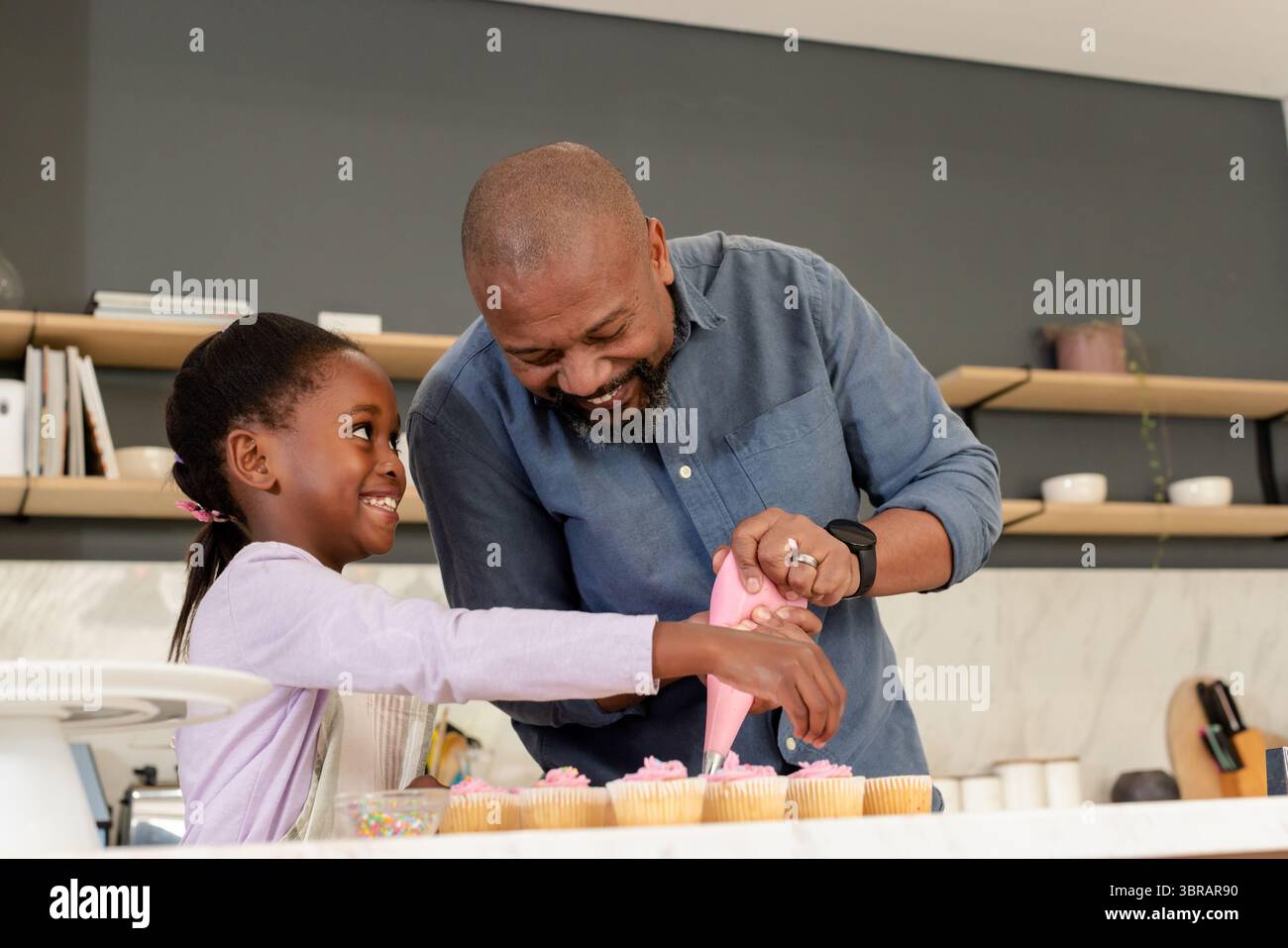 African American father and daughter decorating cupcakes using pink ...
