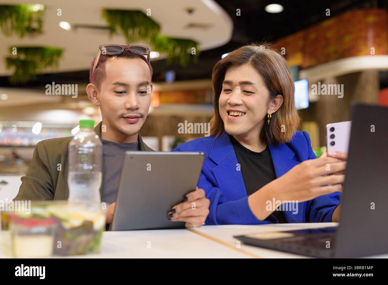 Gender diverse Asian coworkers eating salad and working digitally Stock ...