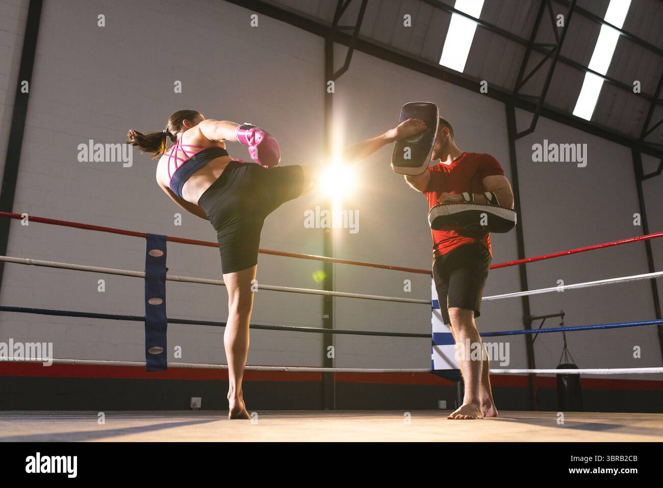 Female trainee wearing pink gloves executing high kick with male coach ...