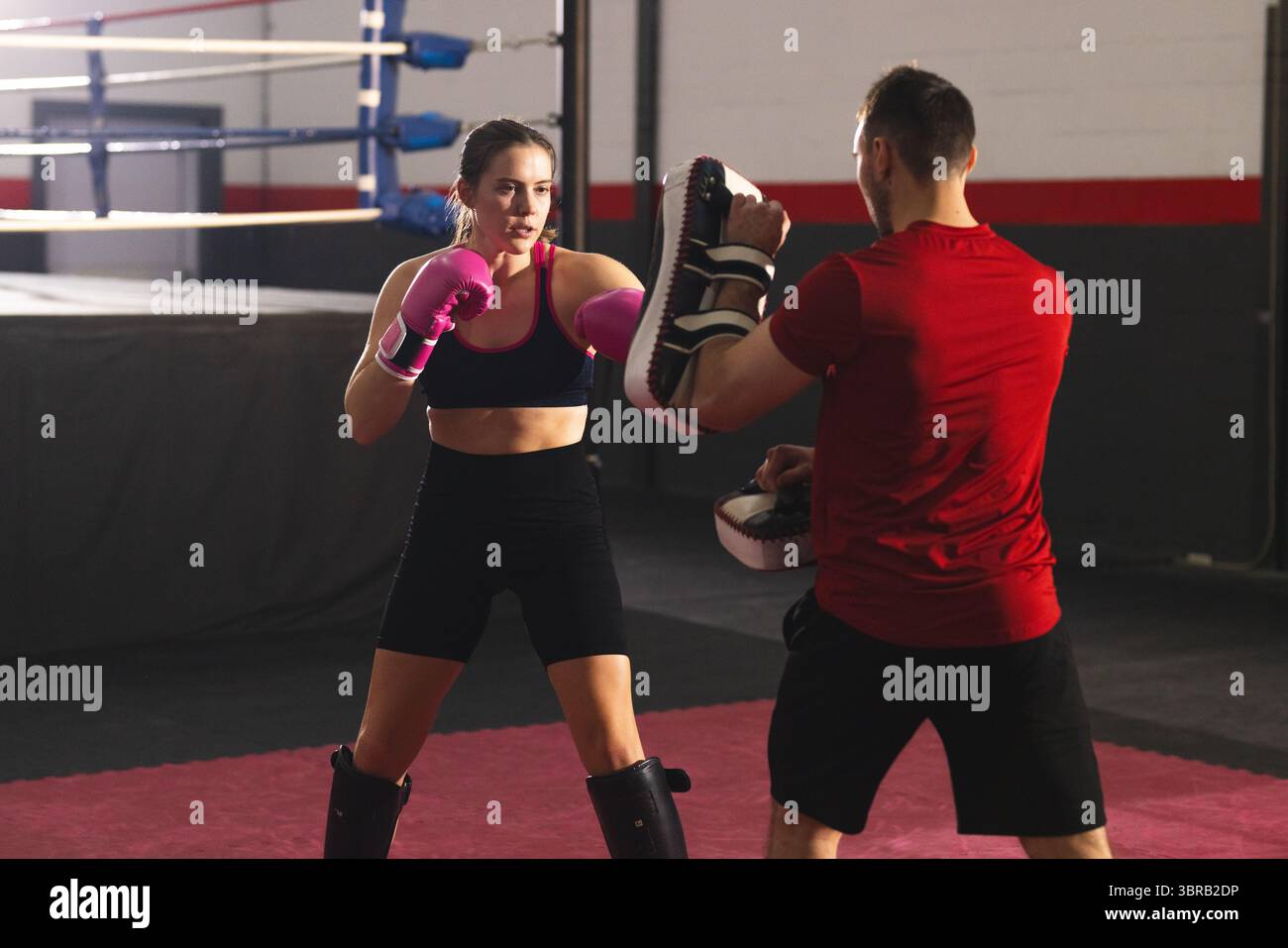Female boxer with pink gloves training with male trainer on padded mat ...
