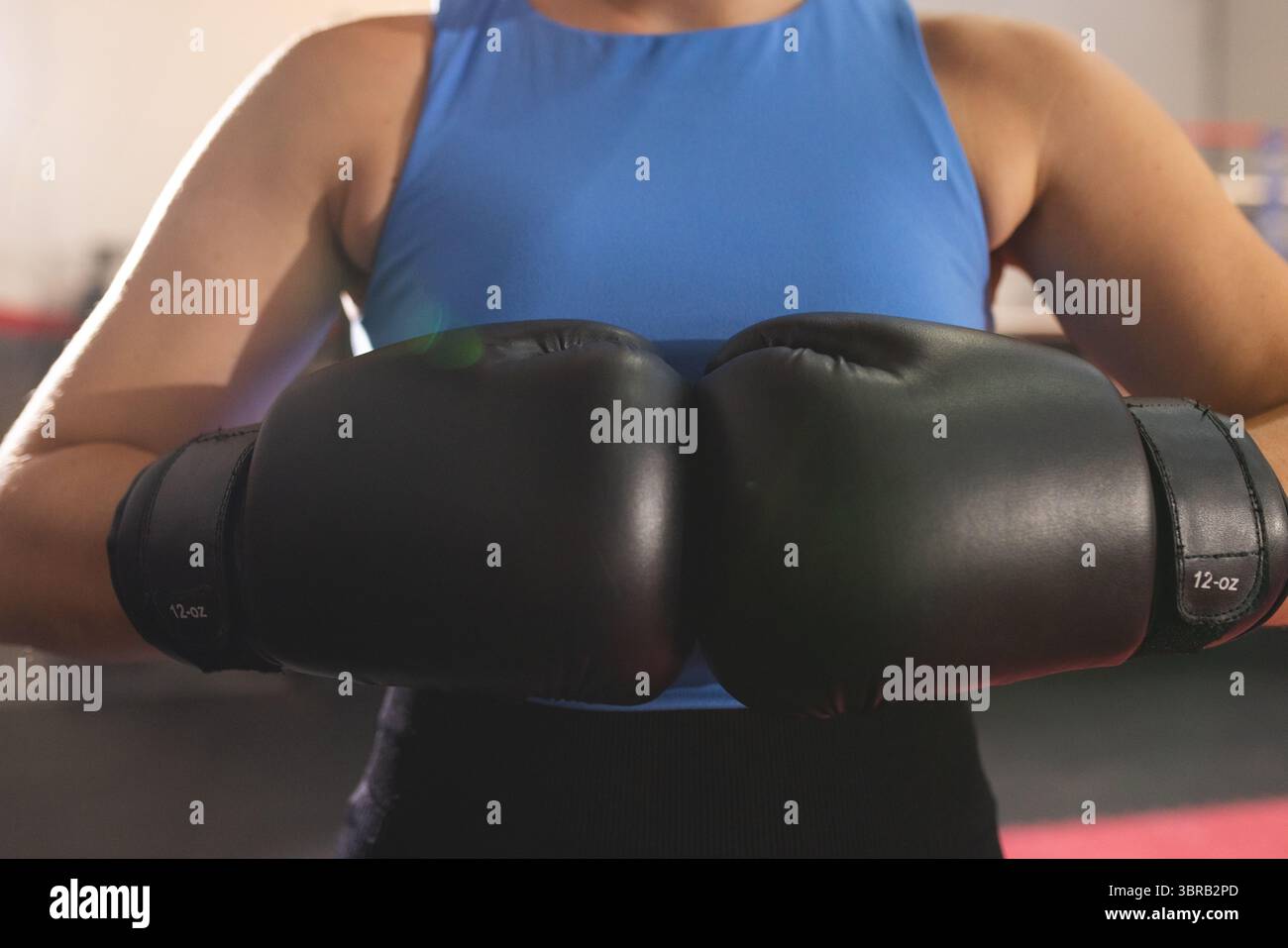 Female athlete wearing blue top and holding black 12oz gloves in boxing ...