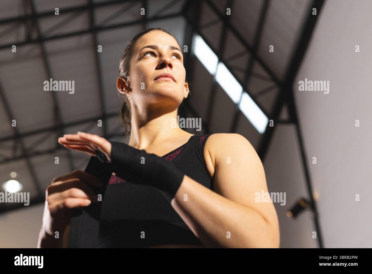 Athletic woman wearing black sports bra wrapping hands with hand wraps ...
