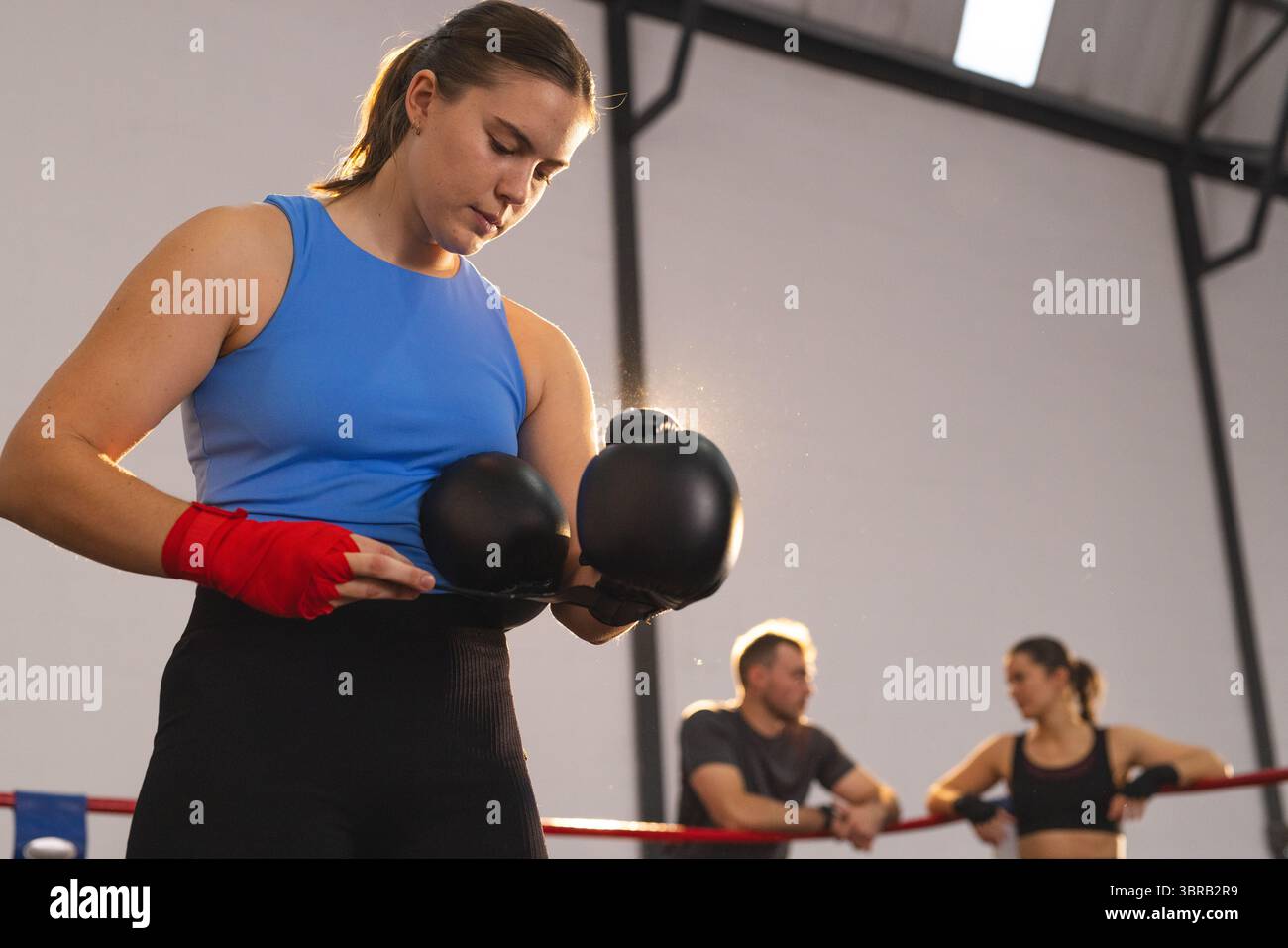 Training partners watching athlete adjusting red wraps, black gloves in boxing ring, copy space ...