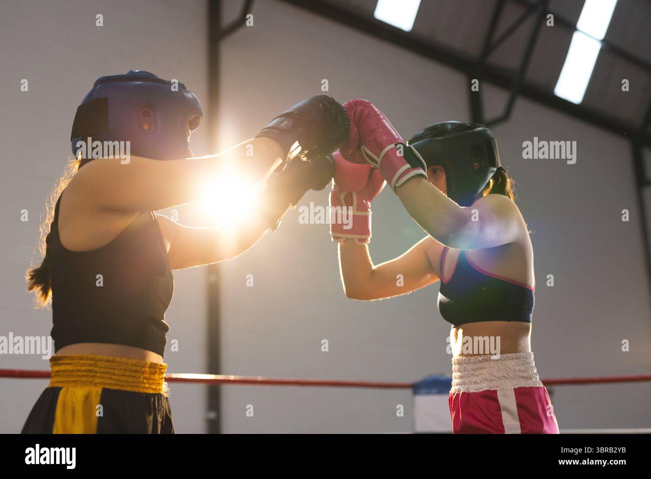 Female boxing trainees sparring in boxing ring, wearing protective headgear and gloves under ...