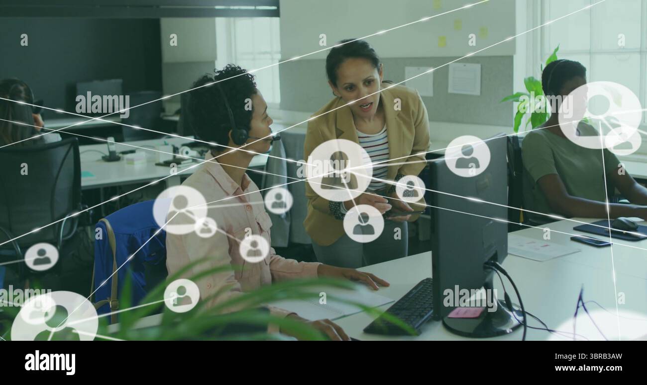 Leaning supervisor guiding seated agent at open office, with computer ...