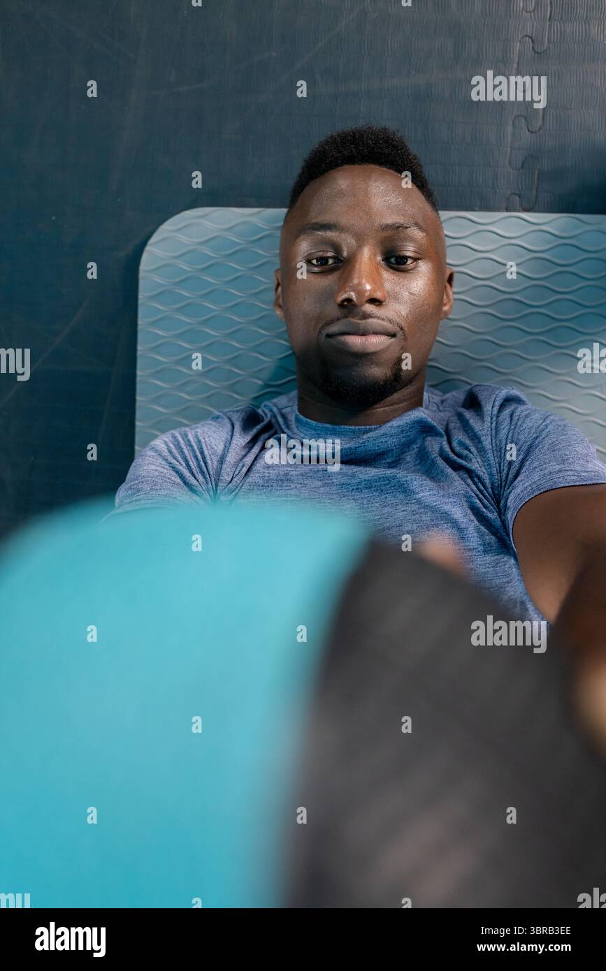 African American man lying on light blue exercise mat above dark foam ...