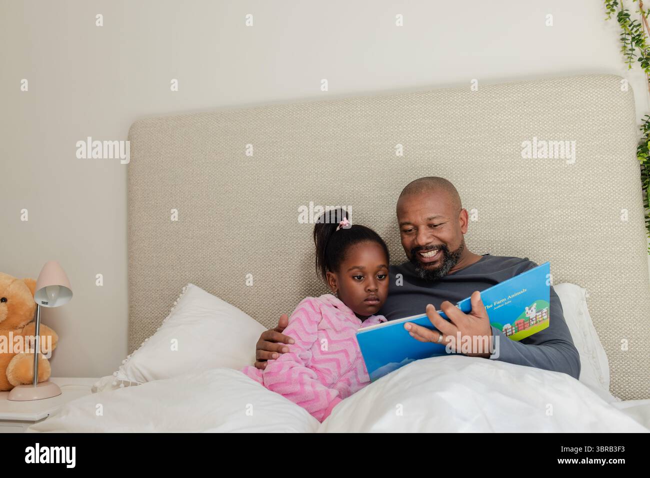 African American father and daughter snuggling on bed reading blue ...