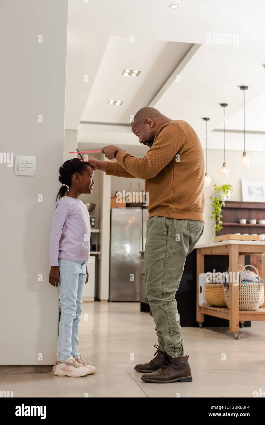 African American father measuring daughter height using red measuring ...