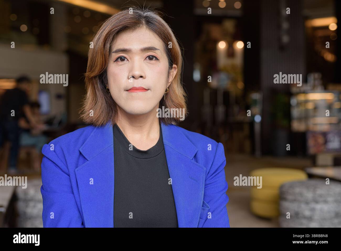 Confident Asian transgender woman in suit sitting alone in coffee shop ...