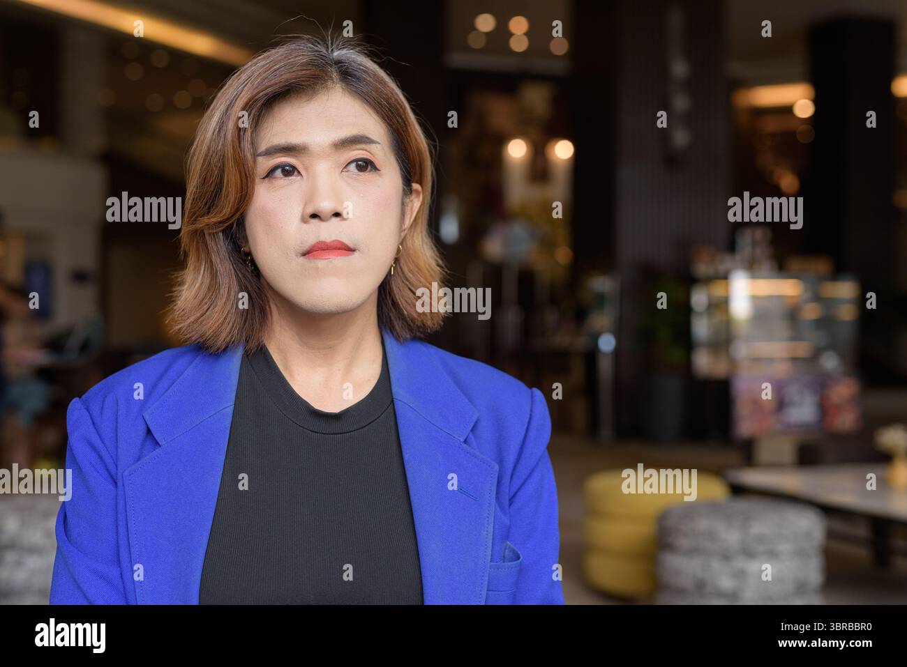 Confident Asian transgender woman in suit sitting alone in coffee shop ...