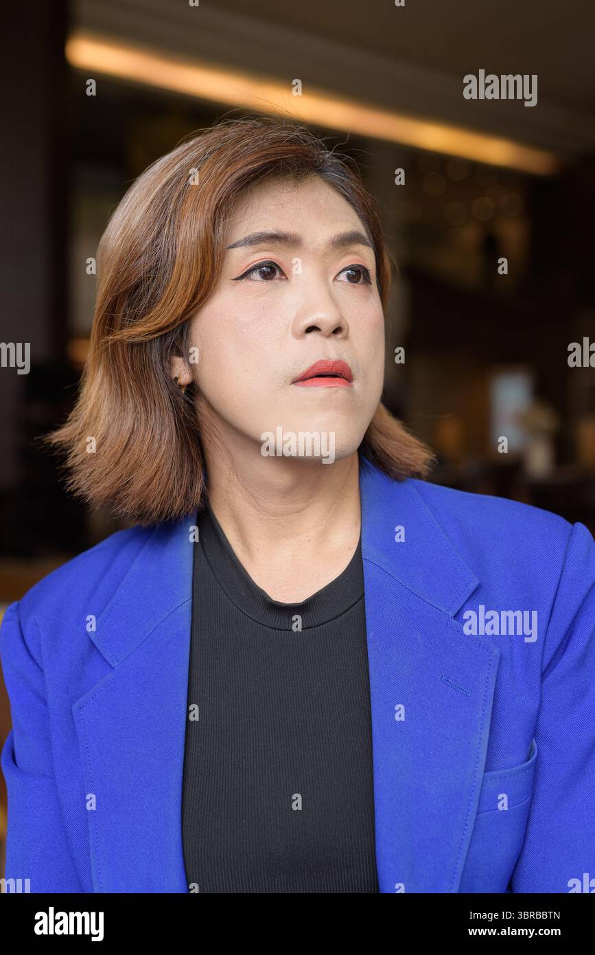 Confident Asian transgender woman in suit sitting alone in coffee shop ...