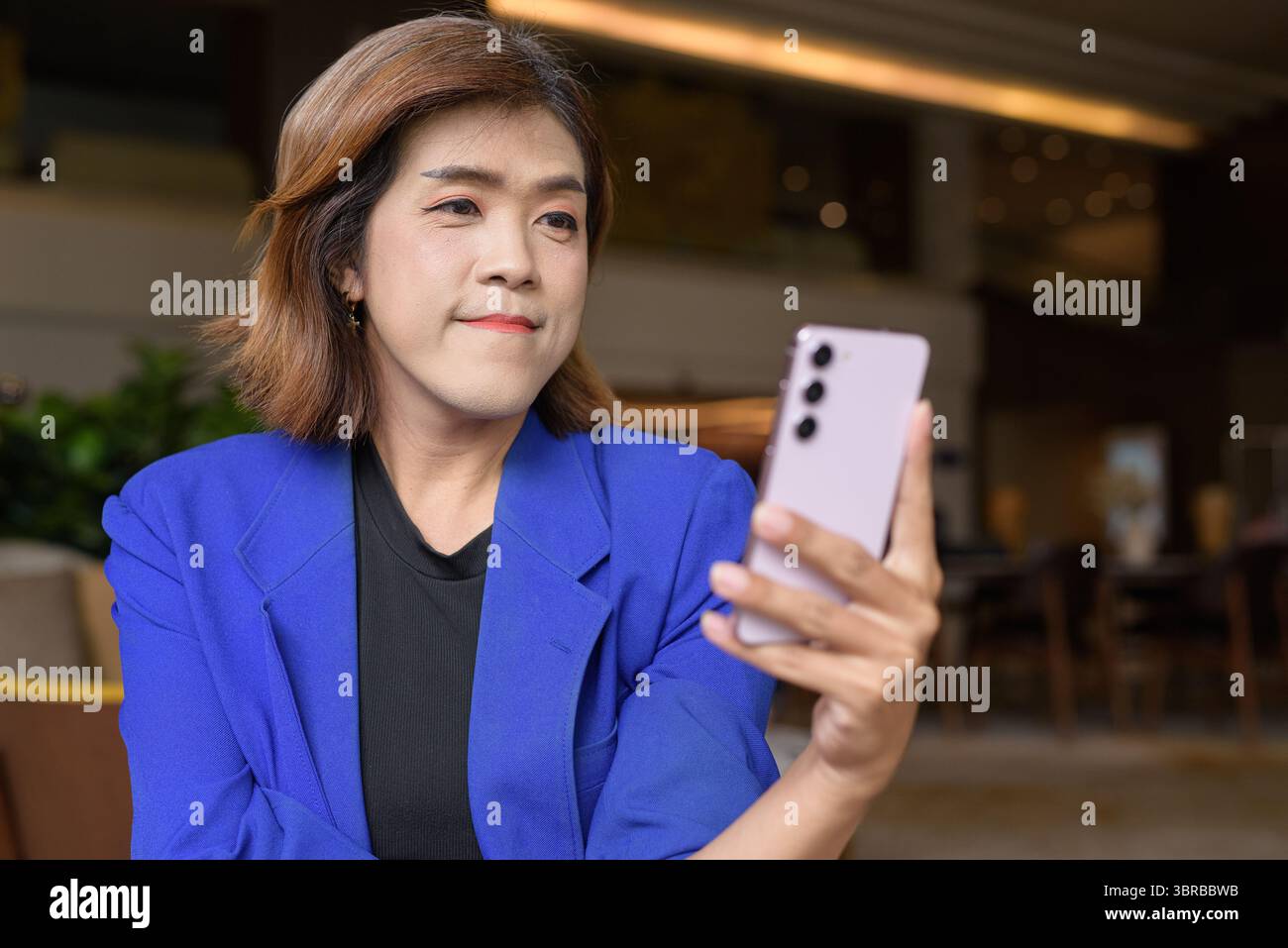 Confident Asian transgender woman in suit sitting alone in coffee shop ...
