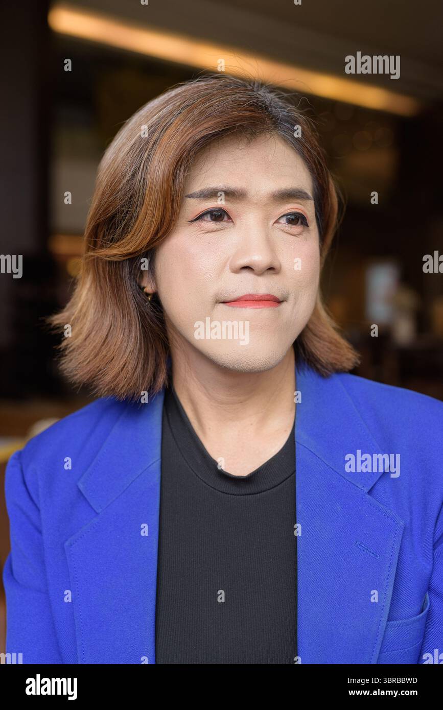 Confident Asian transgender woman in suit sitting alone in coffee shop ...