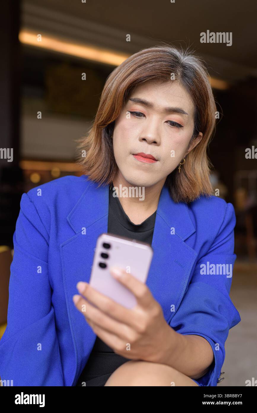 Confident Asian transgender woman in suit sitting alone in coffee shop ...