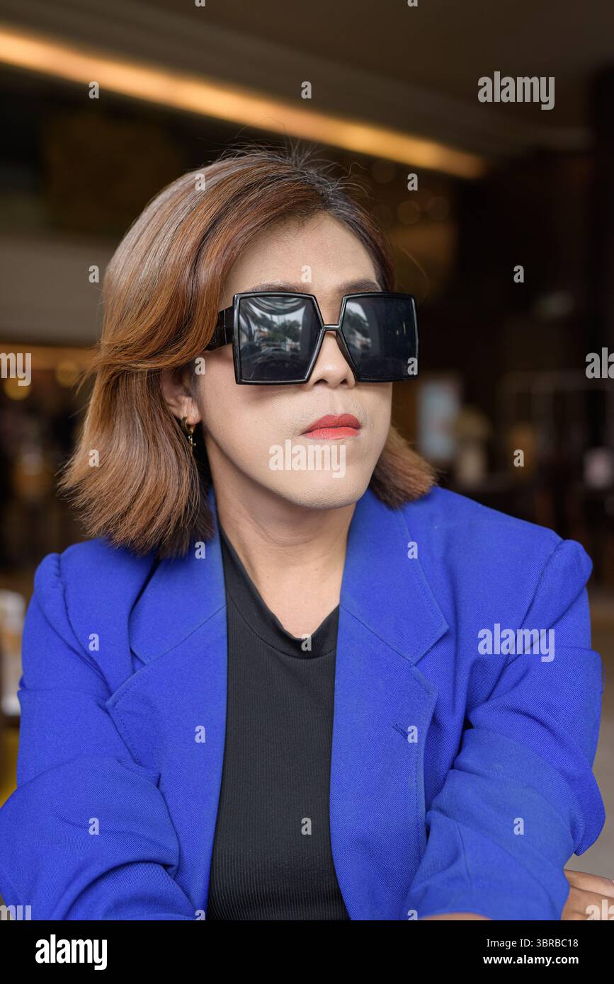 Confident Asian transgender woman in suit sitting alone in coffee shop ...