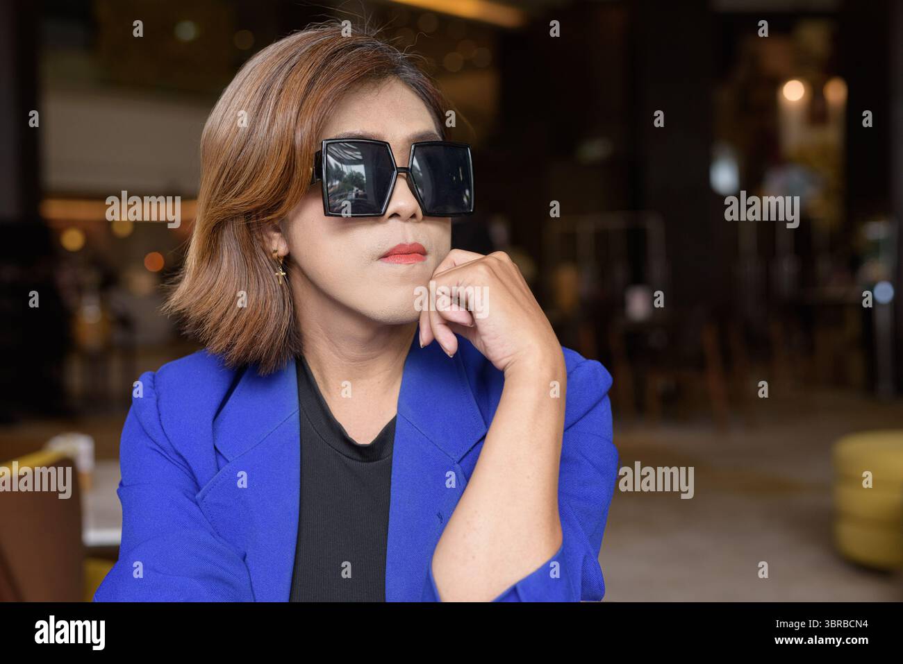 Confident Asian transgender woman in suit sitting alone in coffee shop ...