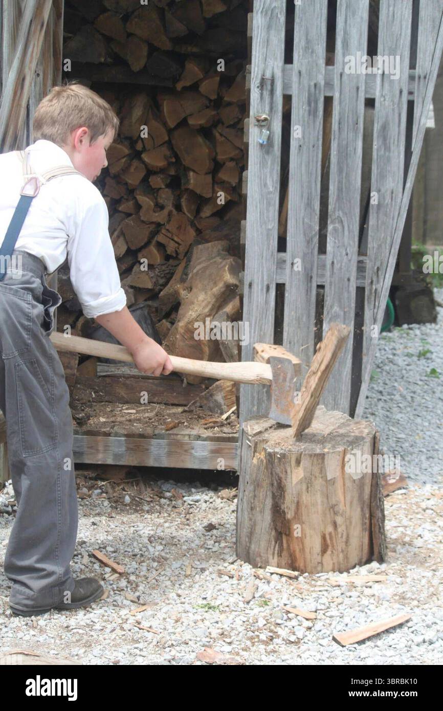 A young Pioneerland reenactor depicts pioneer life by splitting wood at ...