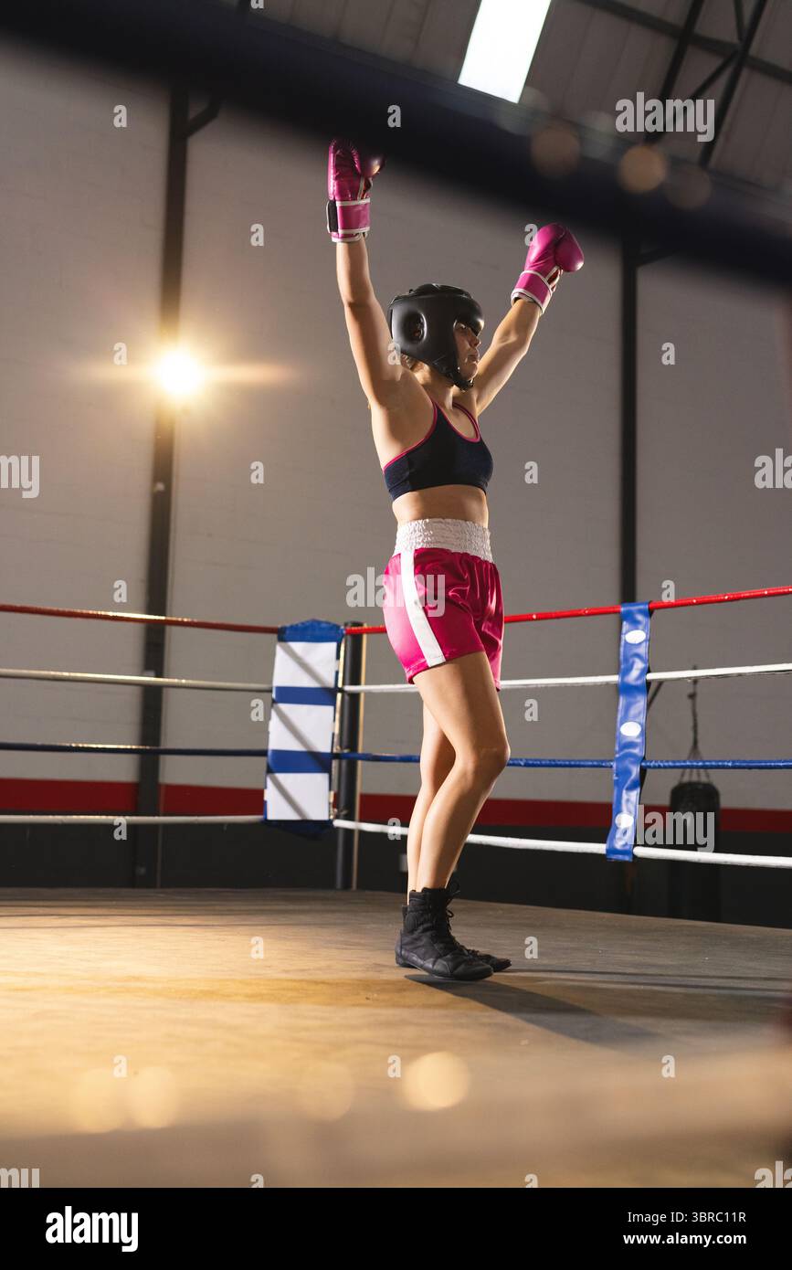 Female boxer standing in boxing ring raising arms in victory wearing ...
