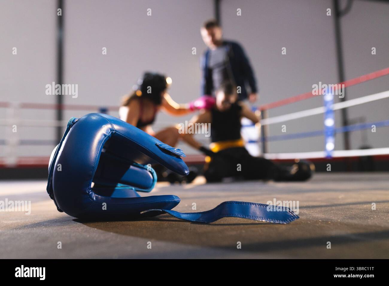 Male coach guiding female boxers inside boxing ring near blue headgear ...