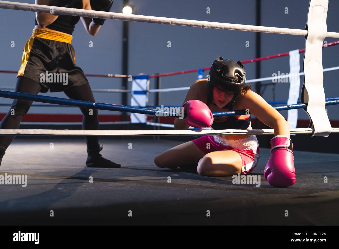 Two female boxers kneeling and standing inside boxing ring at gym with ...