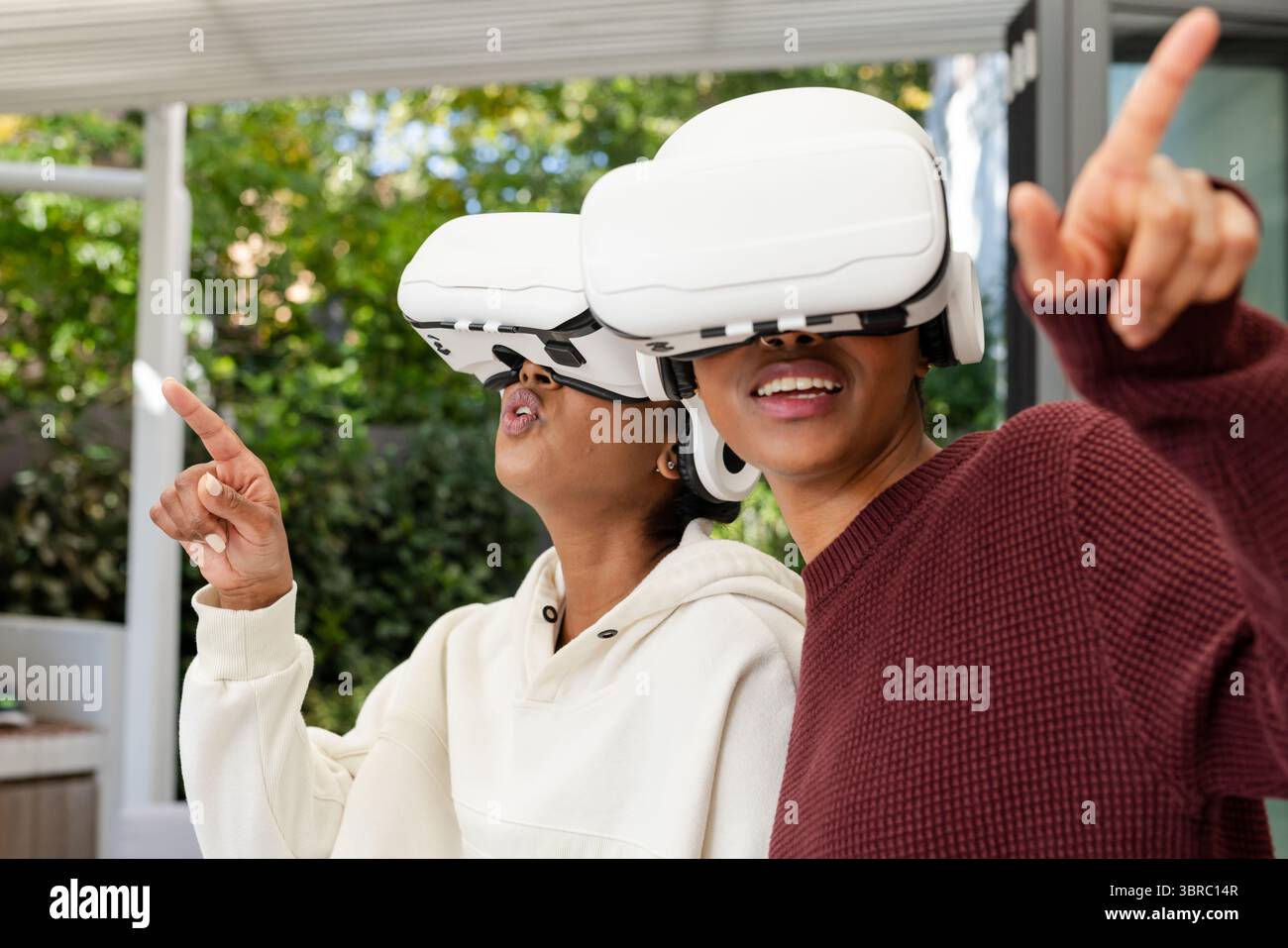 Diverse female friends wearing wireless VR headsets pointing at virtual ...