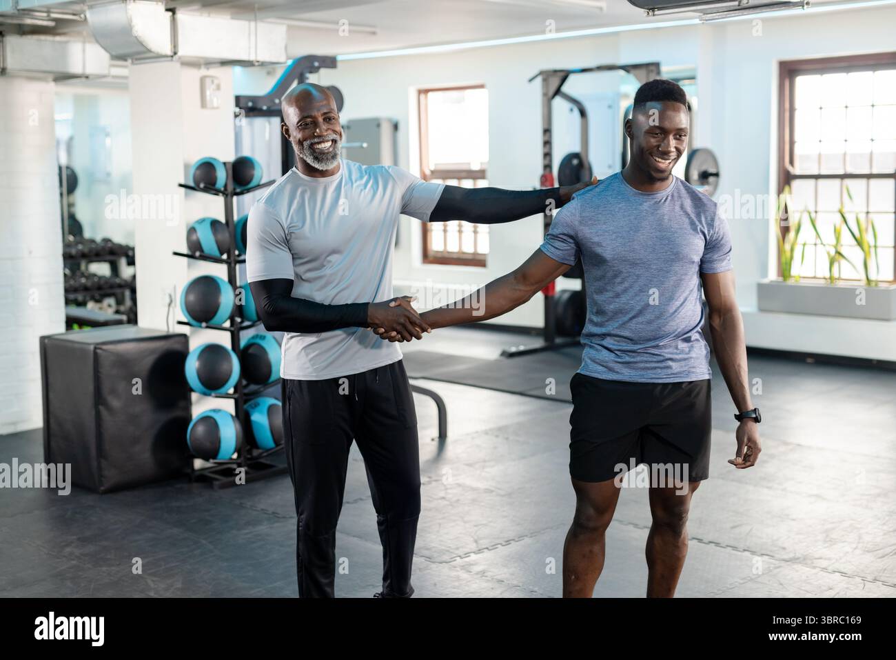 Mature African American trainer and client exchanging handshake at gym ...