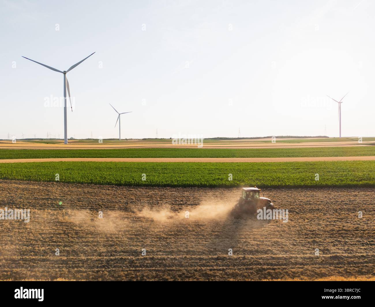 Agricultural tractor is working on the field with wind turbines. Aerial ...