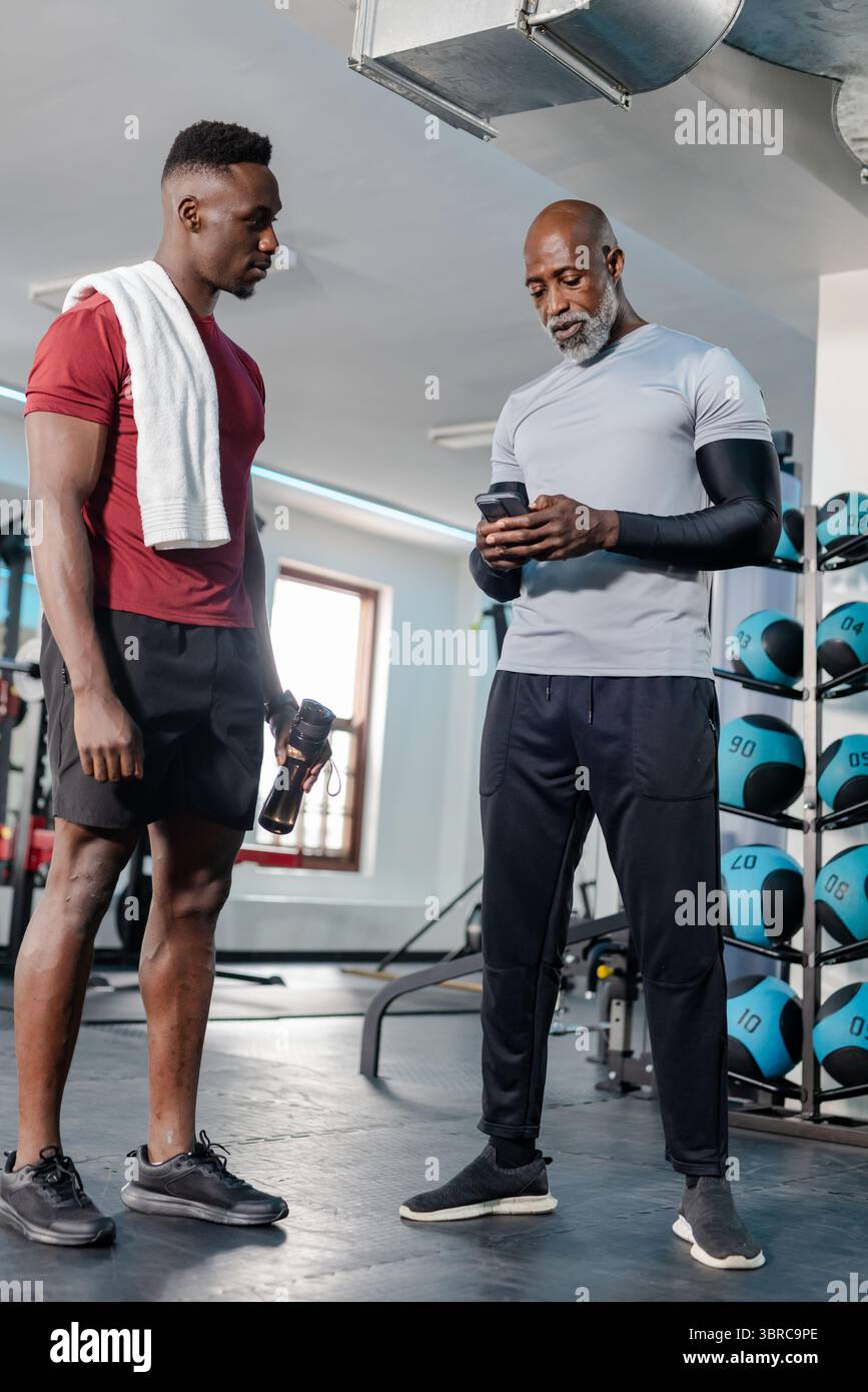 African American trainer and senior client standing in gym holding ...