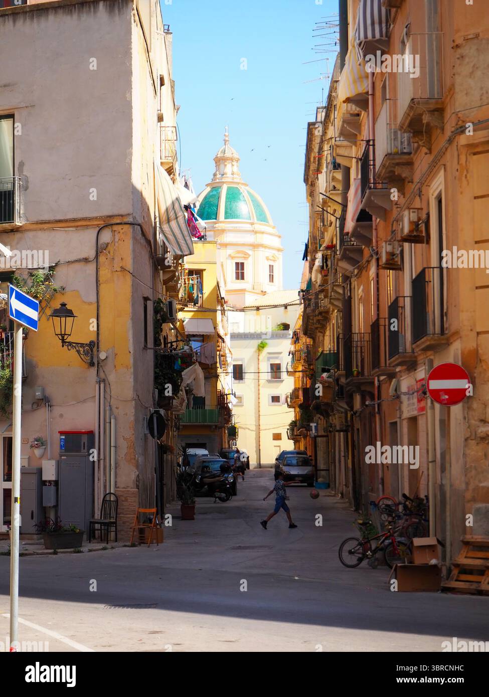 Boy playing football in a narrow street of Palermo with Chiesa del Gesù ...