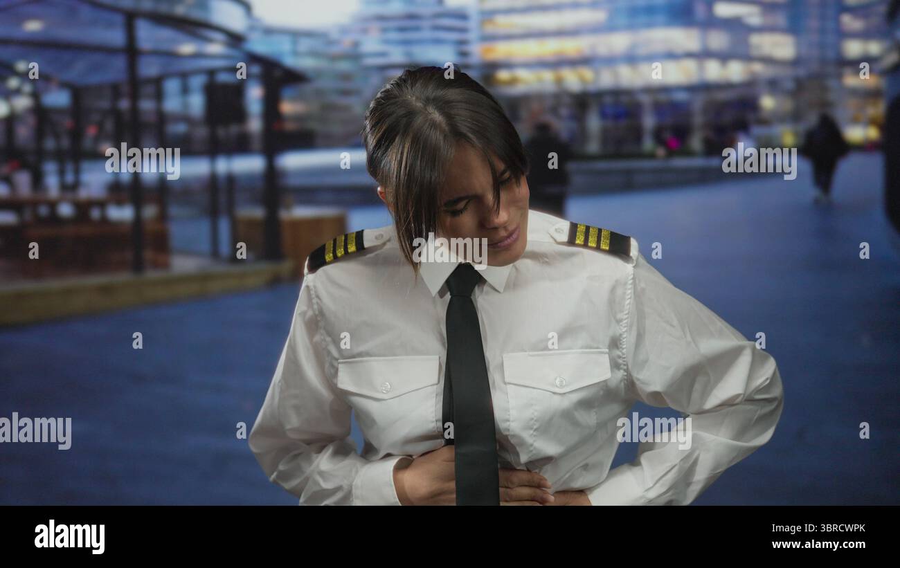 Woman pilot in uniform standing on city street holding her stomach ...