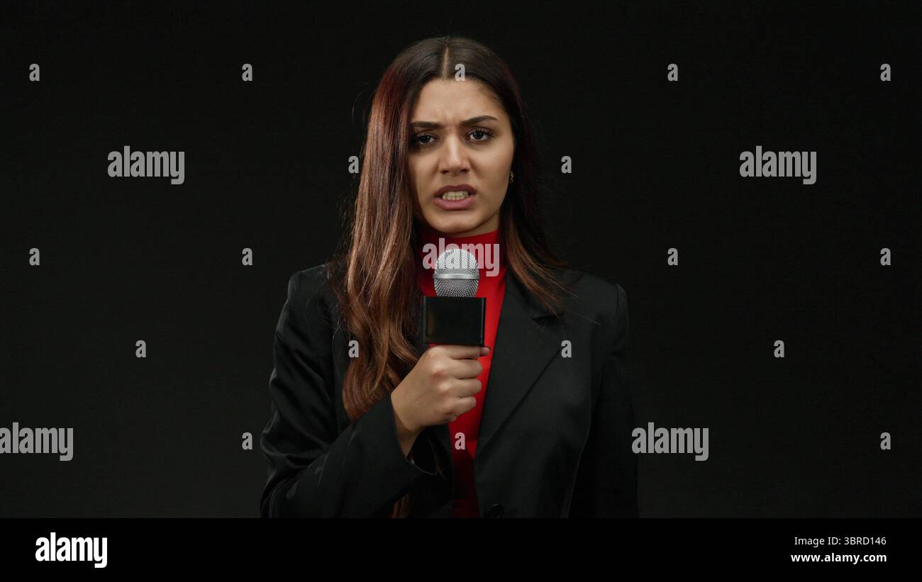 Woman reporter holding microphone against isolated black background ...