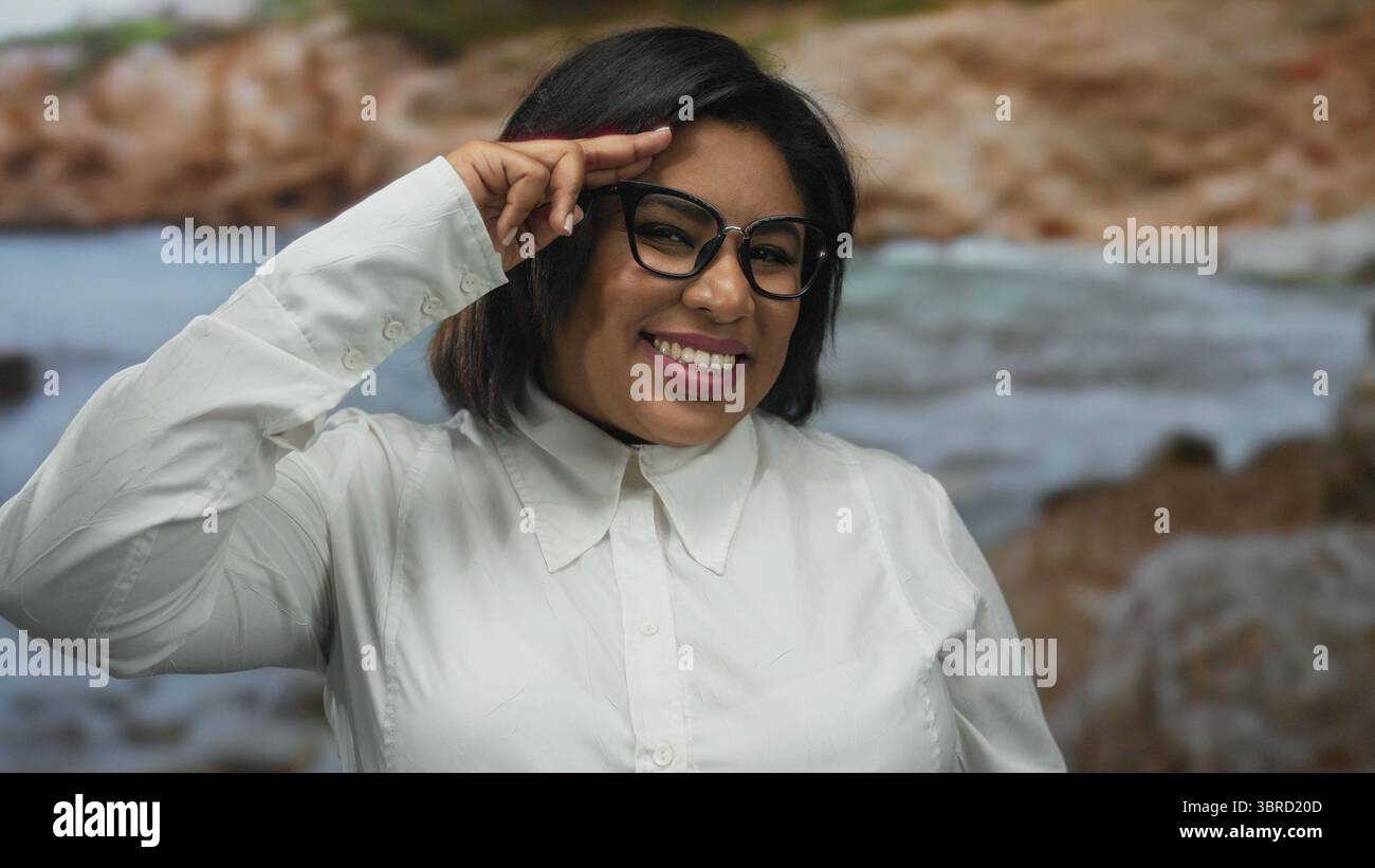 Woman smiling at seaside makes salute gesture wearing glasses with ...