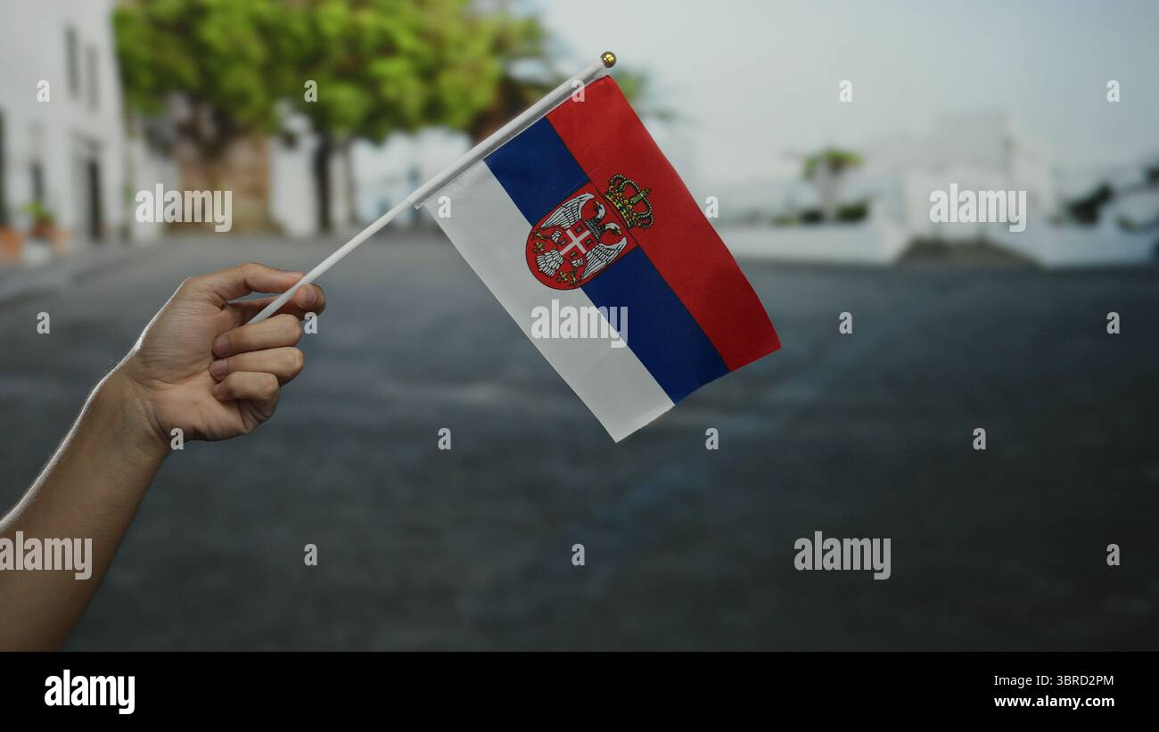 Serbian man holds a serbian flag in his hand against a blurred city ...