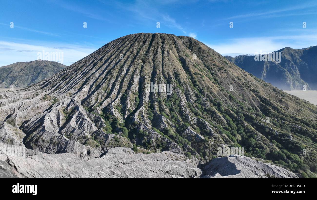 A dramatic view of a volcanic cone with deep vertical ridges carved by ...