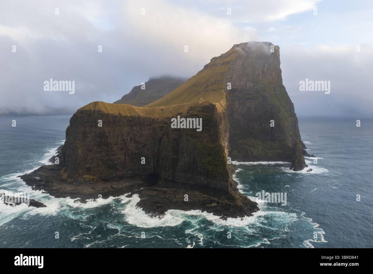 Aerial view of a dramatic, rugged island with steep cliffs and crashing ...