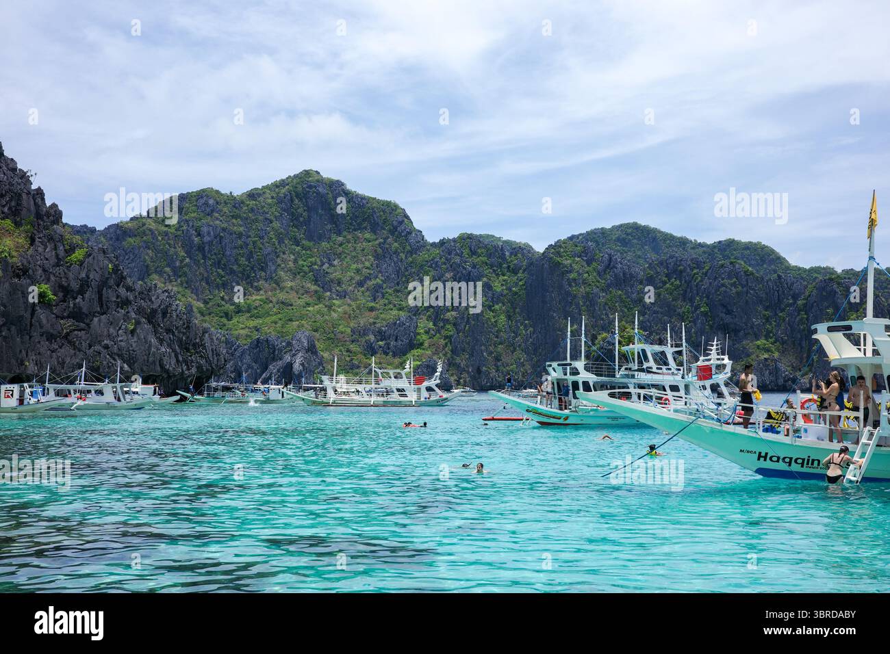 Tour boats and swimmers in tropical lagoon with limestone cliffs. A ...