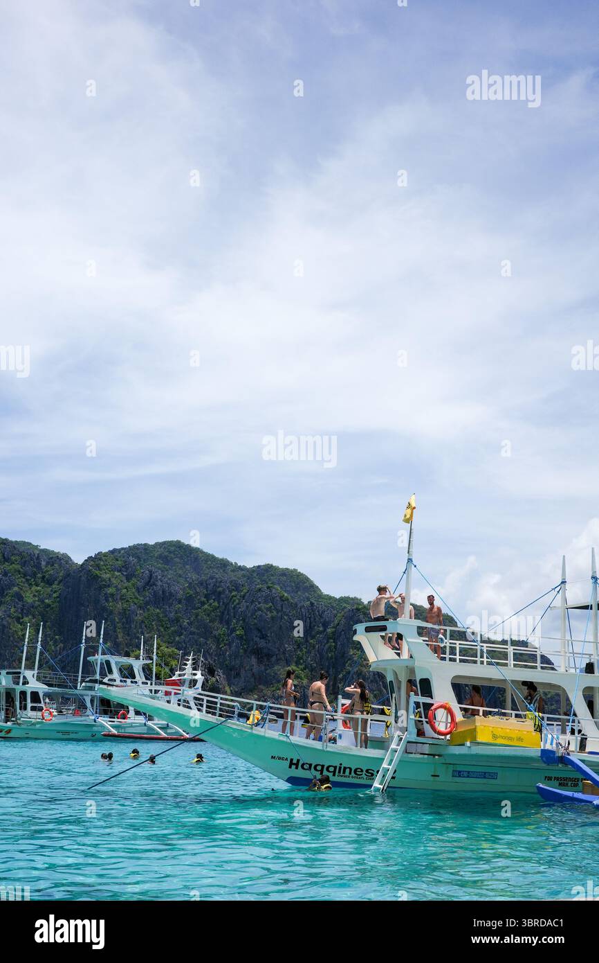 Tour boats and swimmers in a tropical lagoon with limestone cliffs. A ...