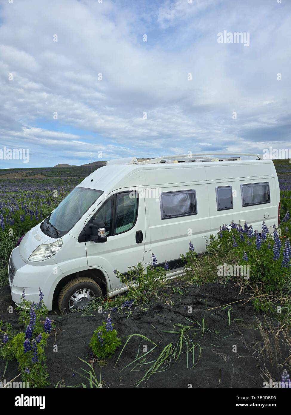 A white camper van is partially submerged in soft black sand in Iceland ...