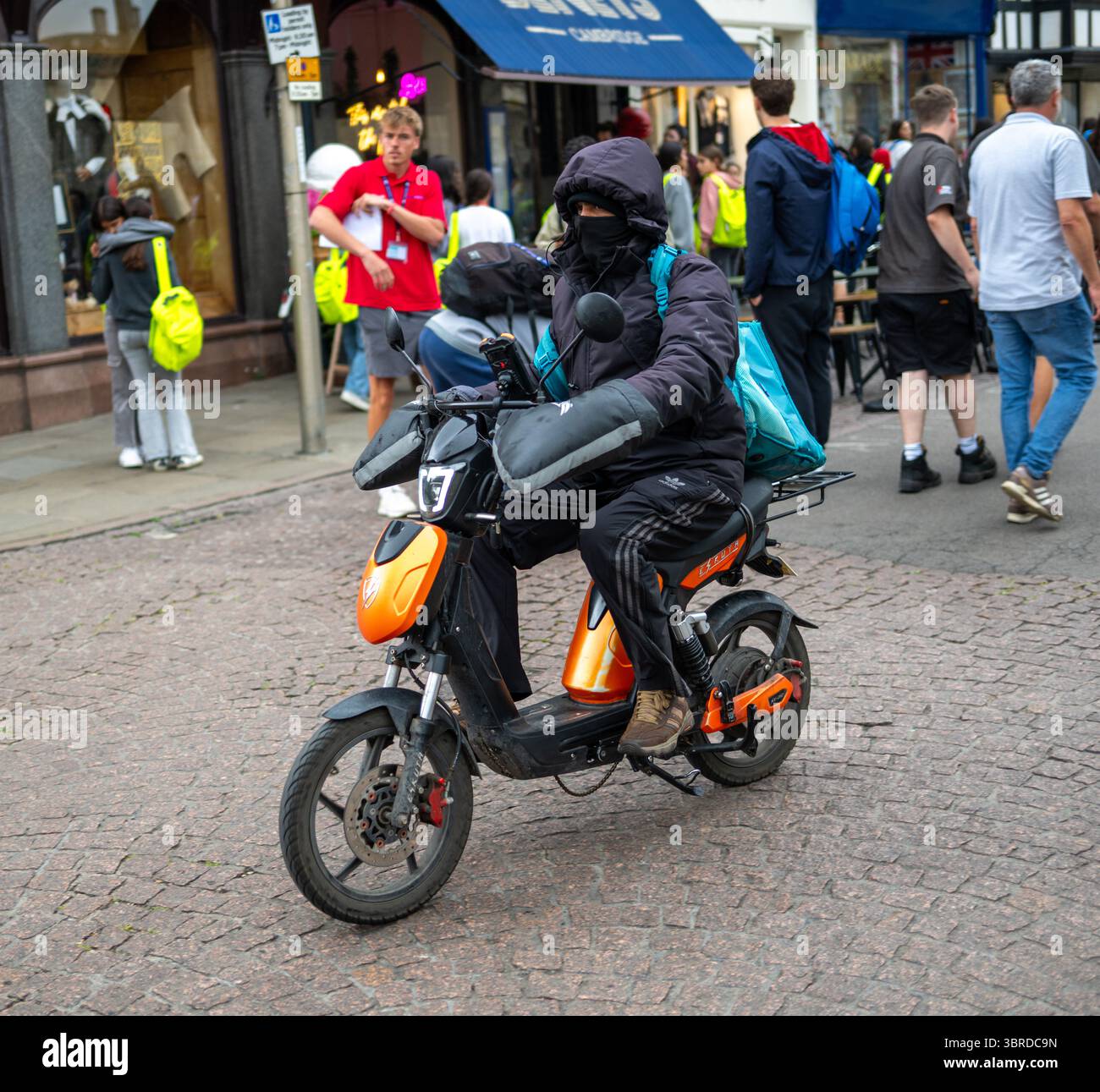 Delivery rider on an electric scooter wearing dark clothing and a face ...