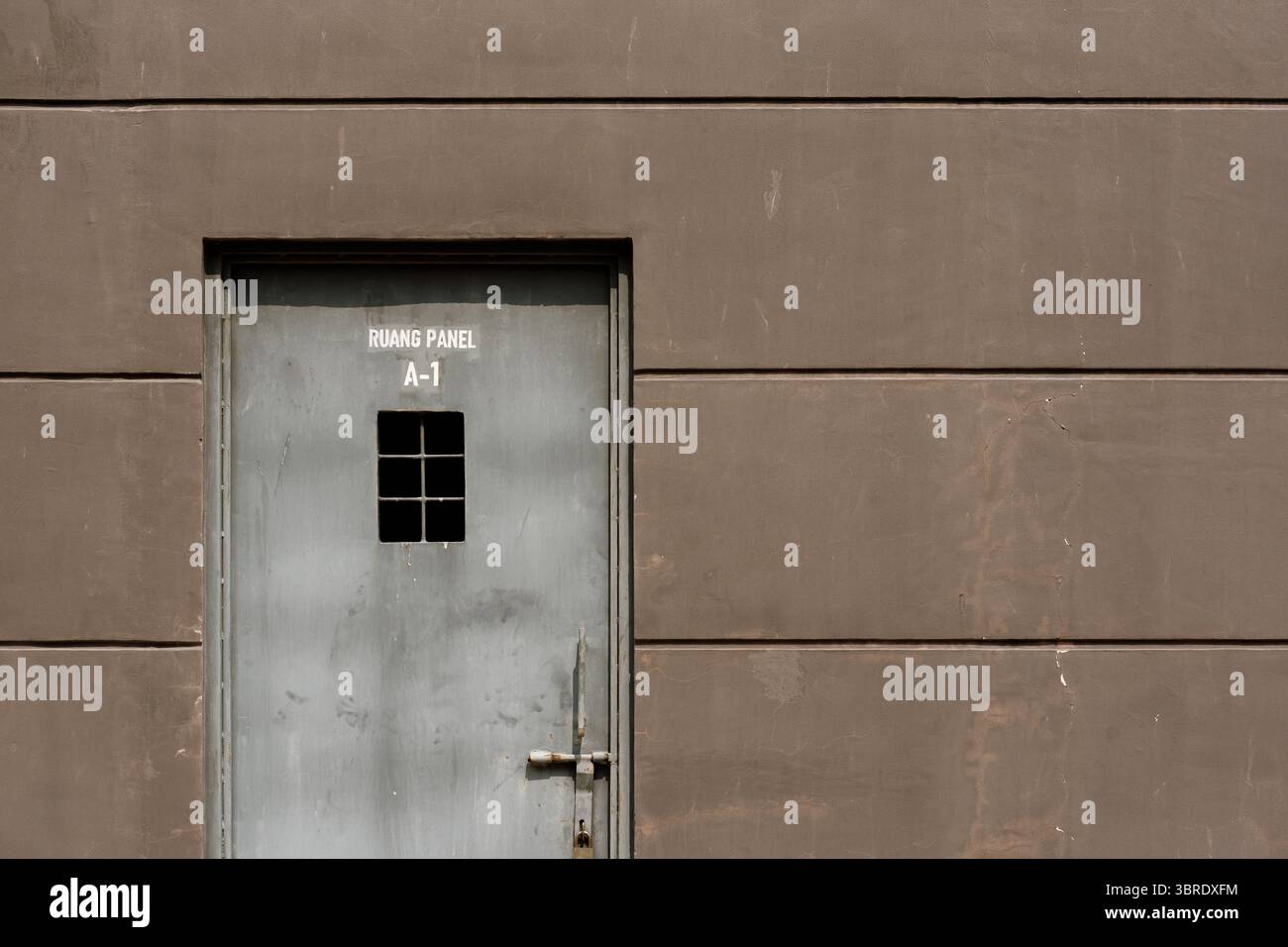 Close-up of a weathered gray industrial metal door labeled 'RUANG PANEL ...