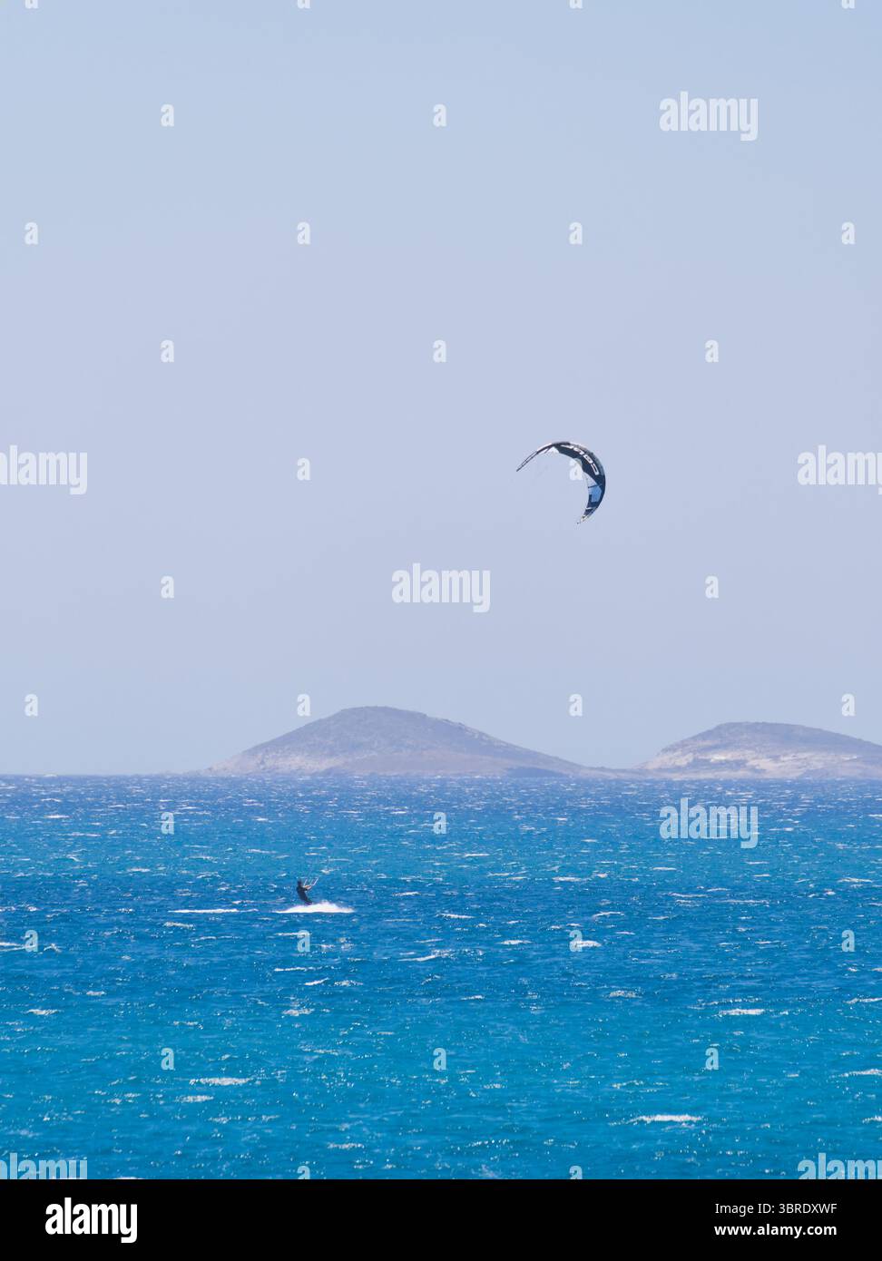 A kitesurfer rides across bright blue waters with distant islands on ...