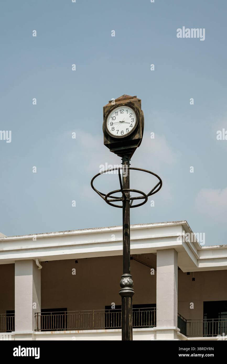 A vintage public clock on a black metal pole stands before a classic ...