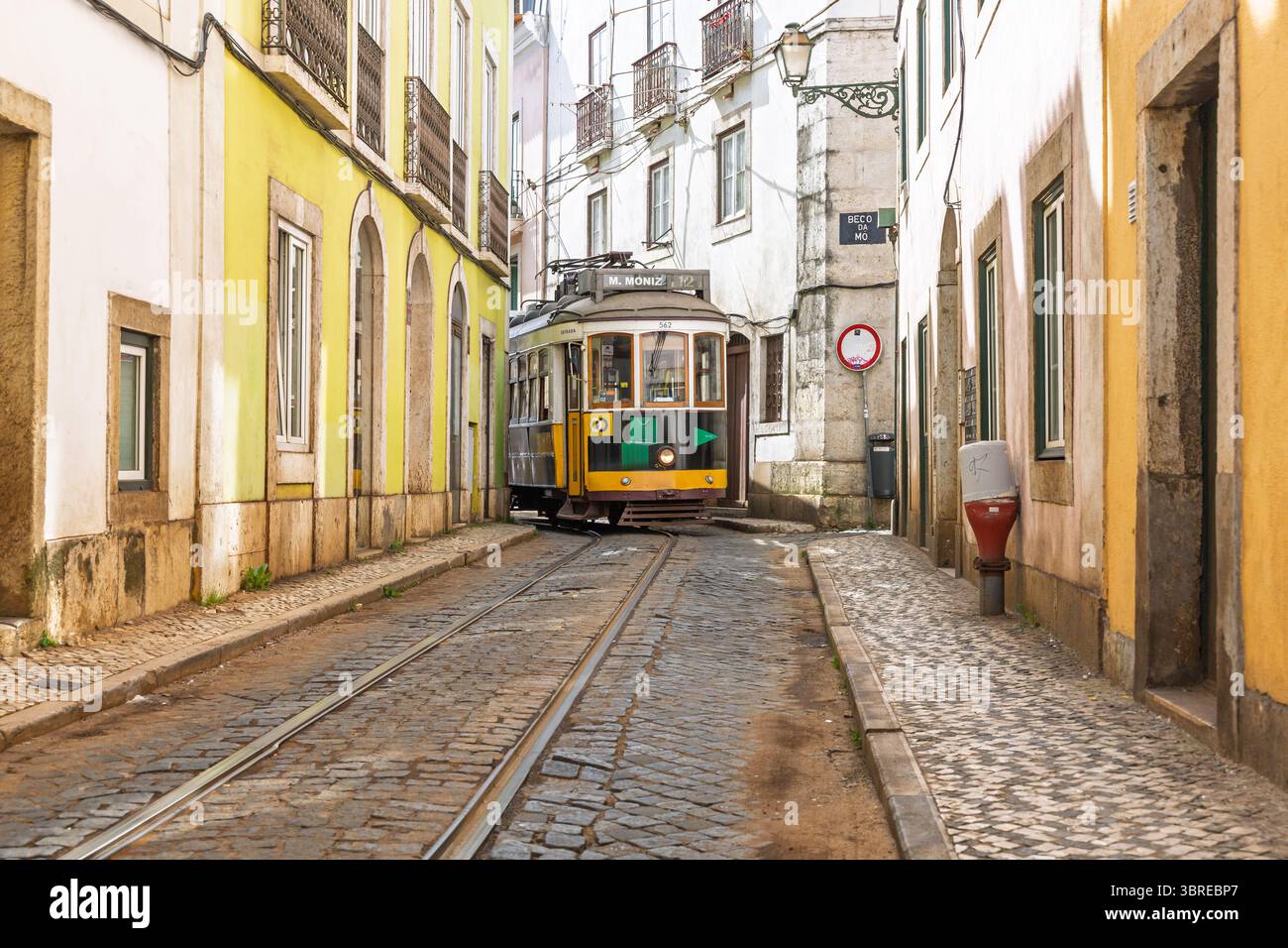 An iconic yellow tram navigates a charming cobblestone street in Lisbon ...